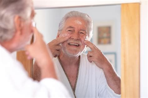 Premium Photo | Skin care handsome senior man applying cream at his face and looking at himself ...