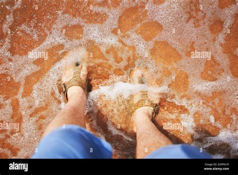 Men's feet in sandals on beach. Man in jeans shorts stands and looks ...